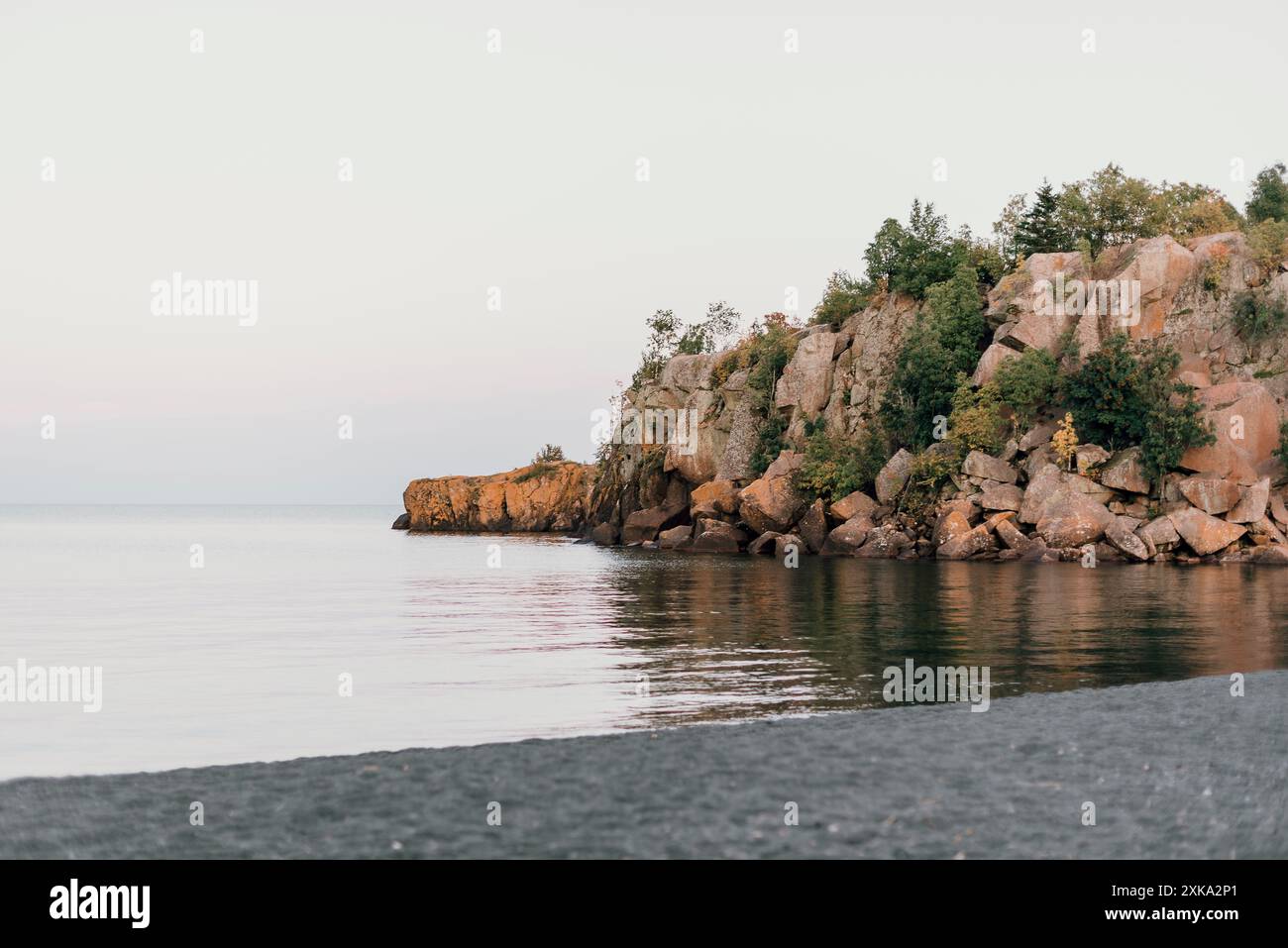 Rocky cliffside by calm water at twilight Stock Photo - Alamy