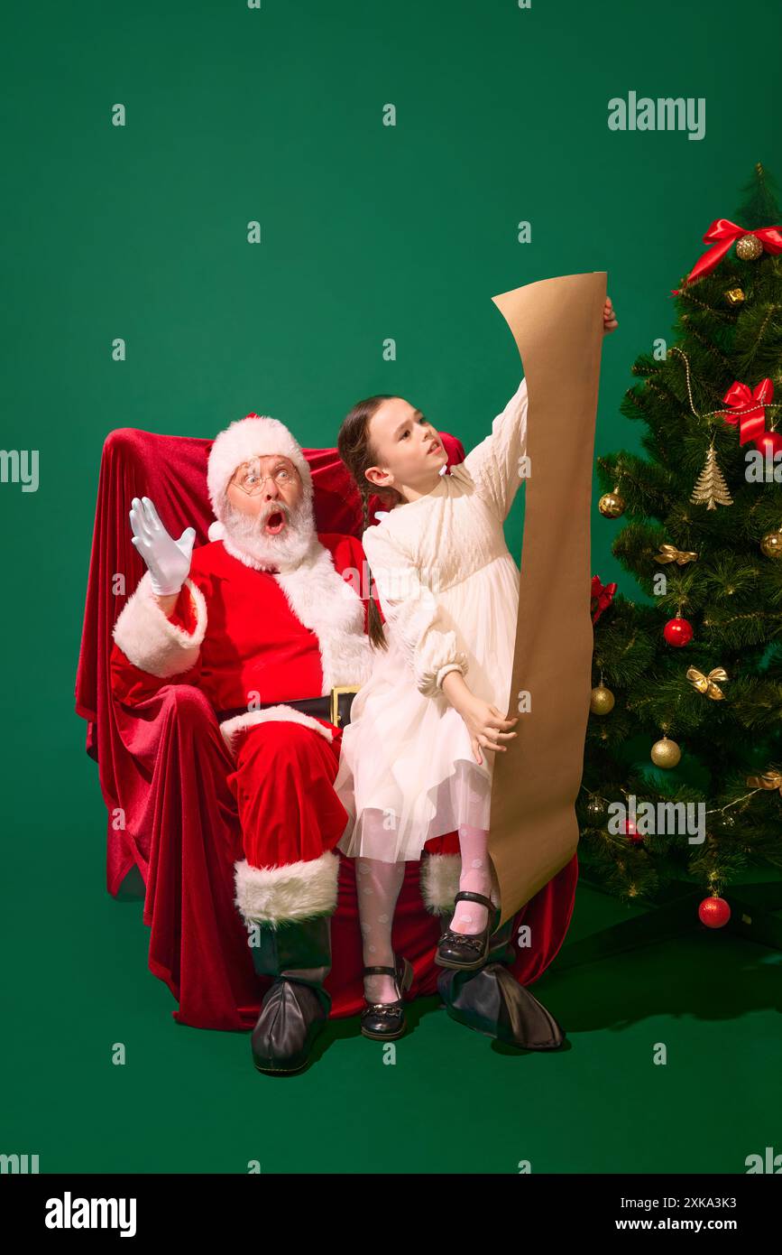 Surprised Santa sitting with girl, child reading long wish list beside ...
