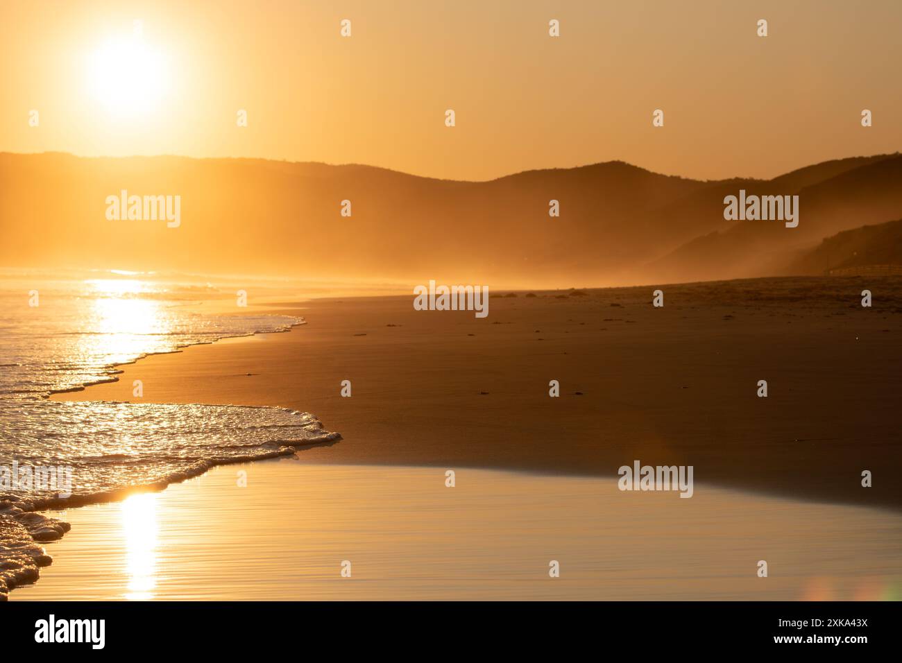 Golden hour over tranquil beach with gentle waves and misty horizon ...