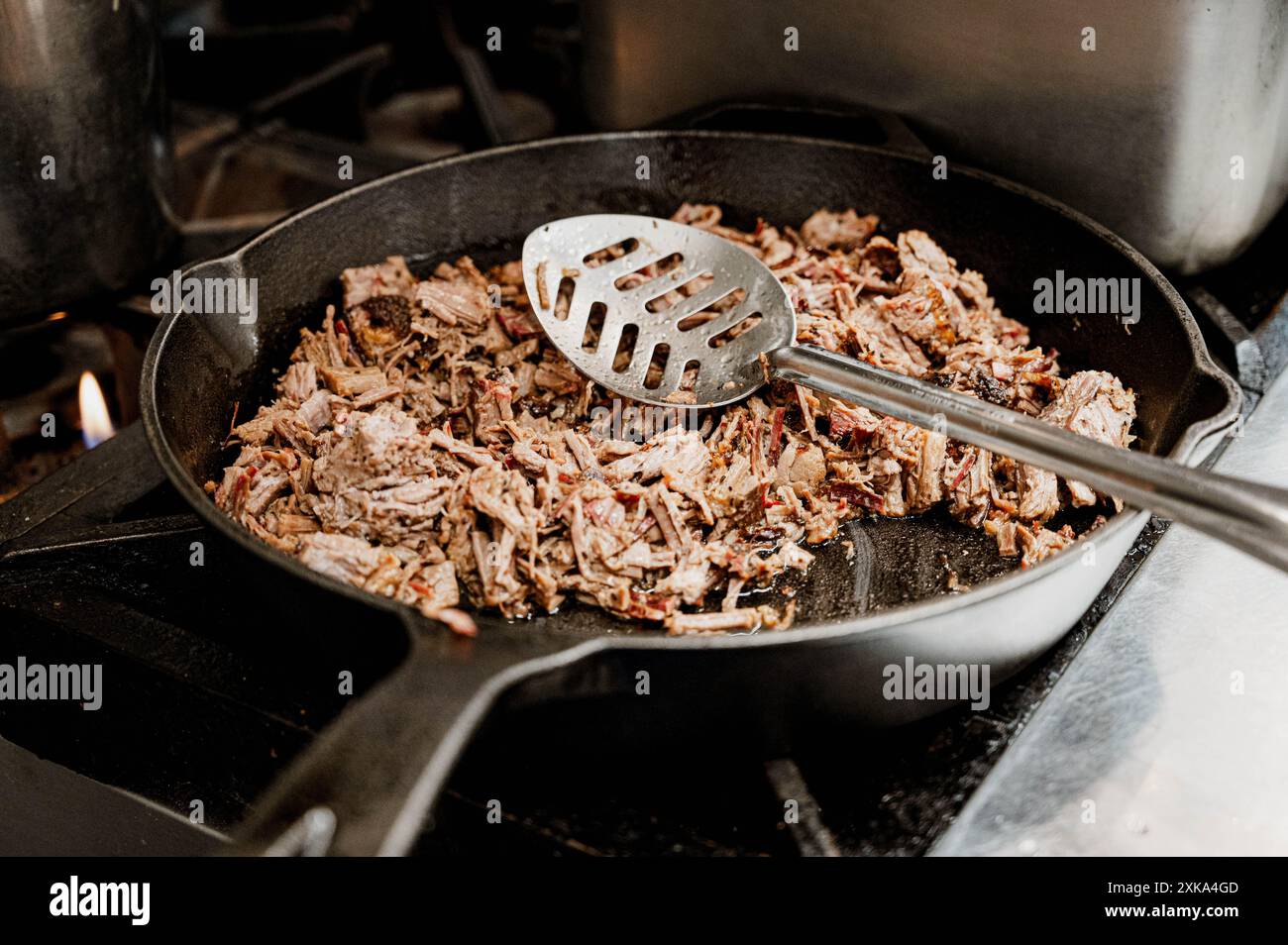 skillet of pulled meat with giant metal spoon sitting on stove top ...