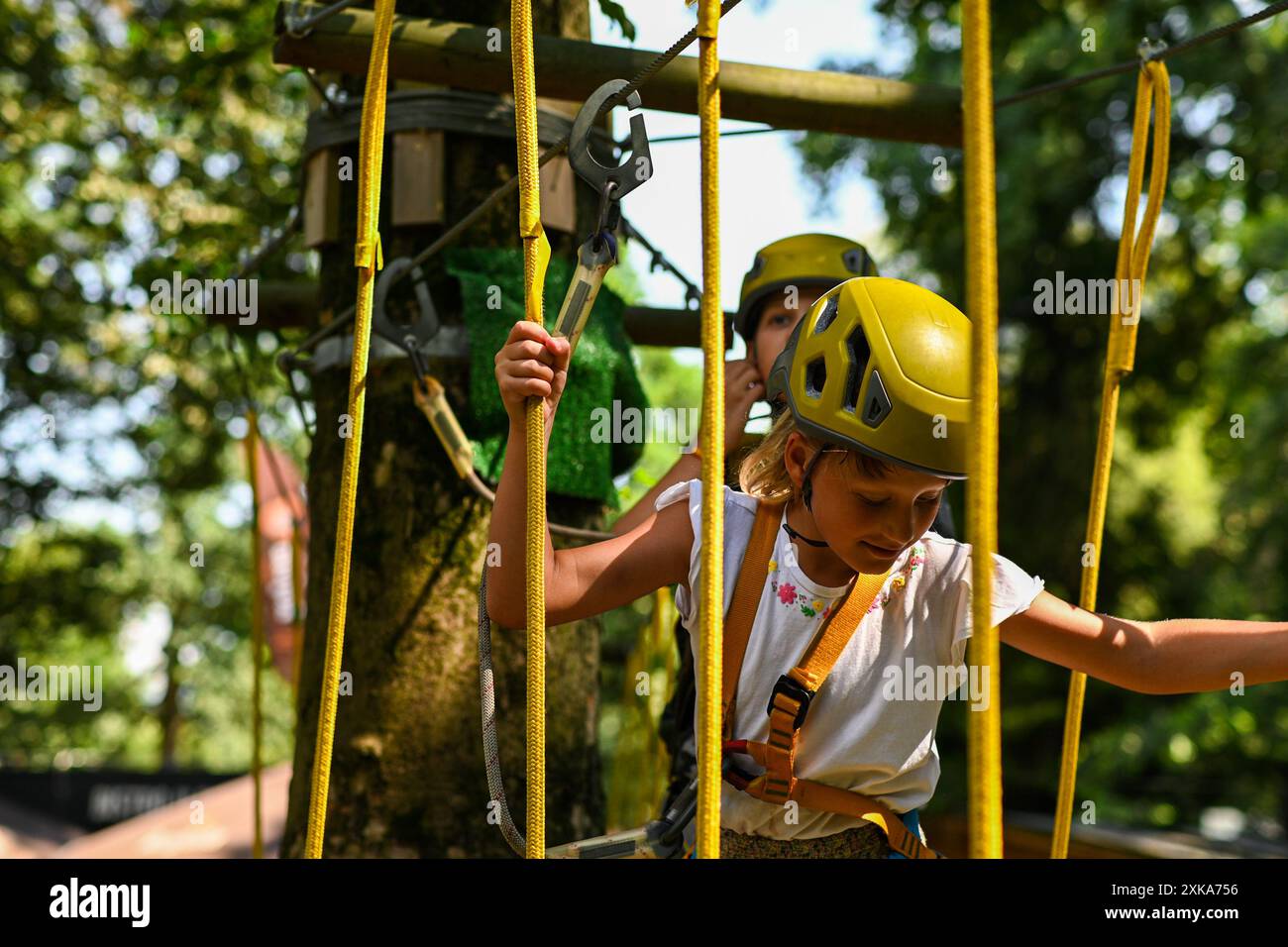 Two children wearing safety harnesses and helmets navigating a rope ...