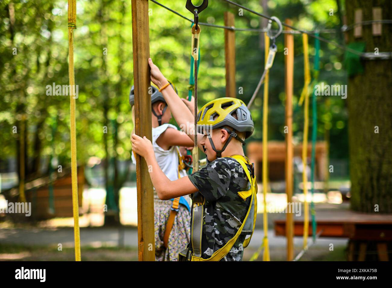 Two children wearing safety harnesses and helmets navigating a rope ...