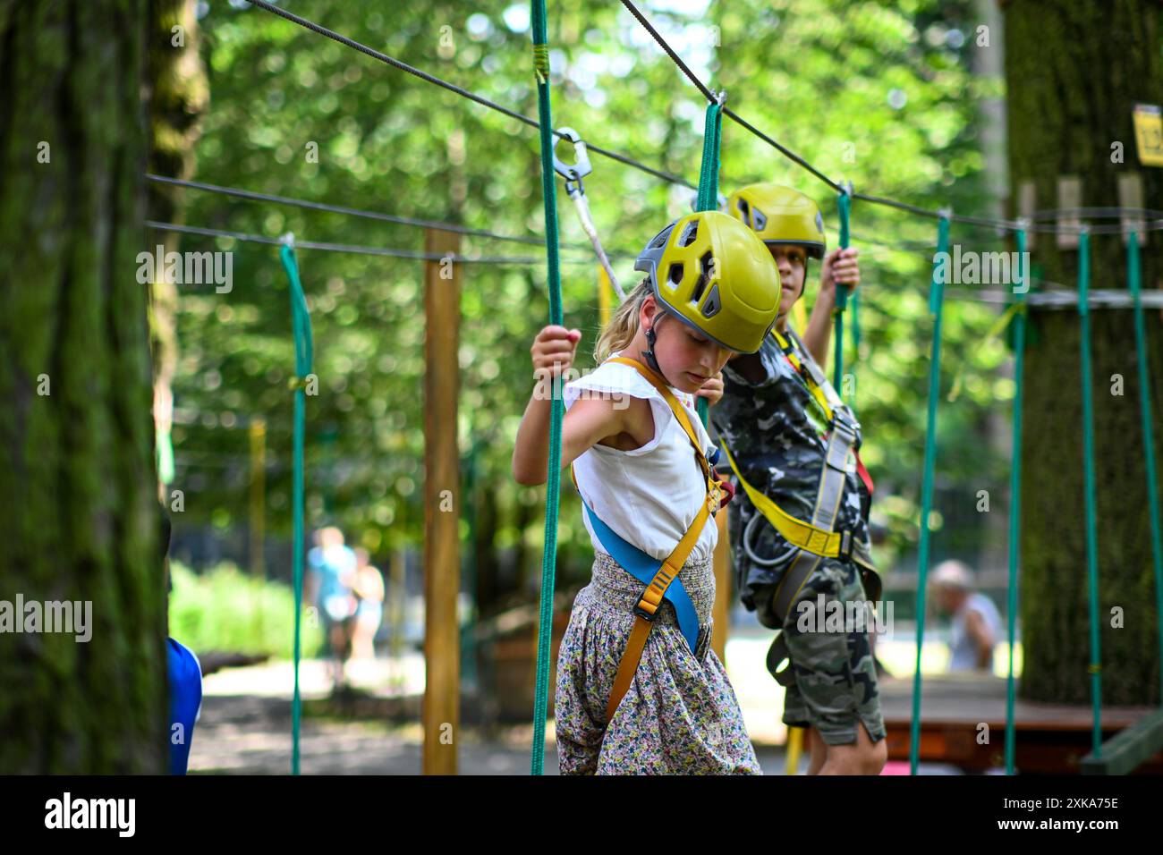 Two children wearing safety harnesses and helmets navigating a rope ...