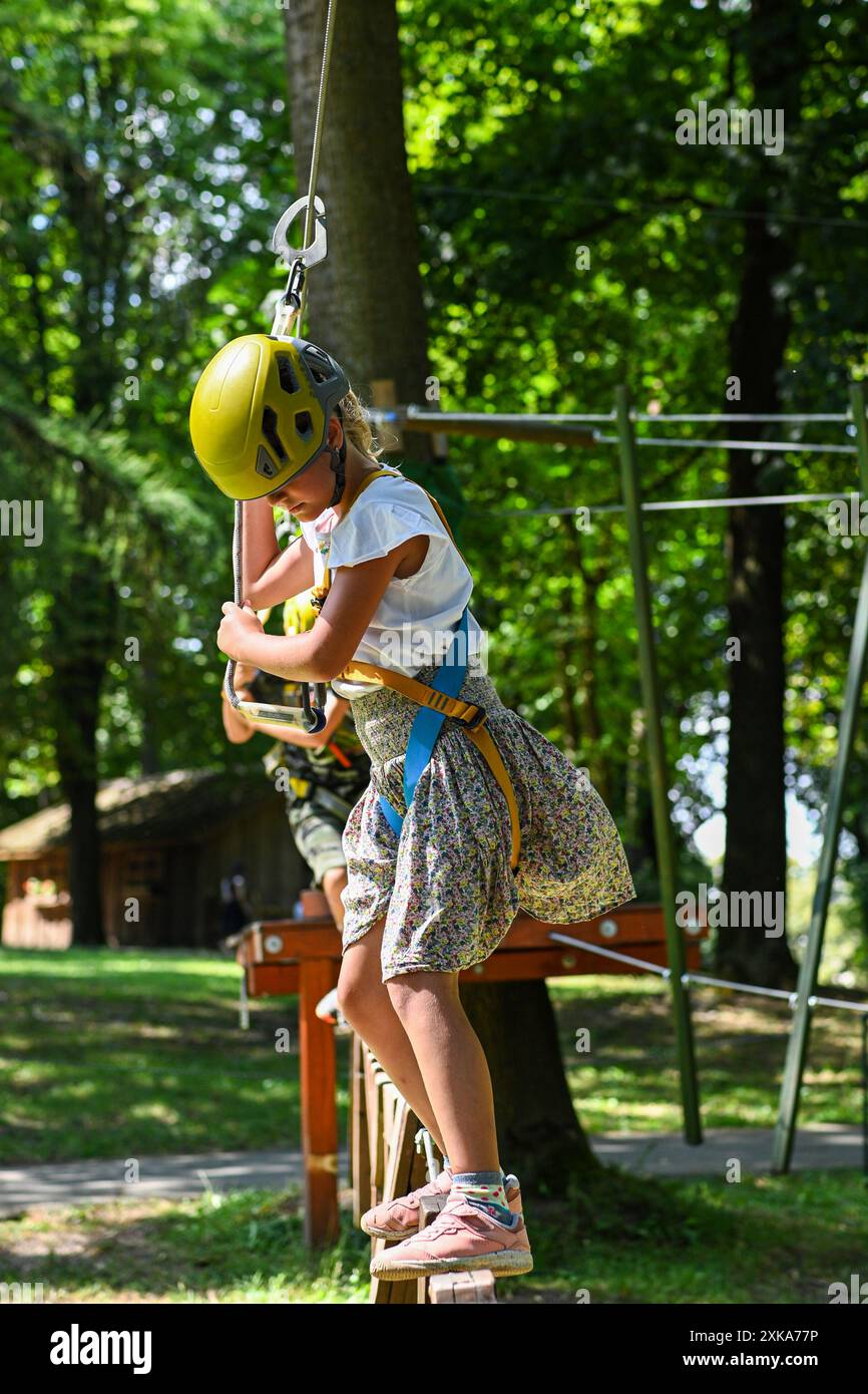Two children wearing safety harnesses and helmets navigating a rope ...