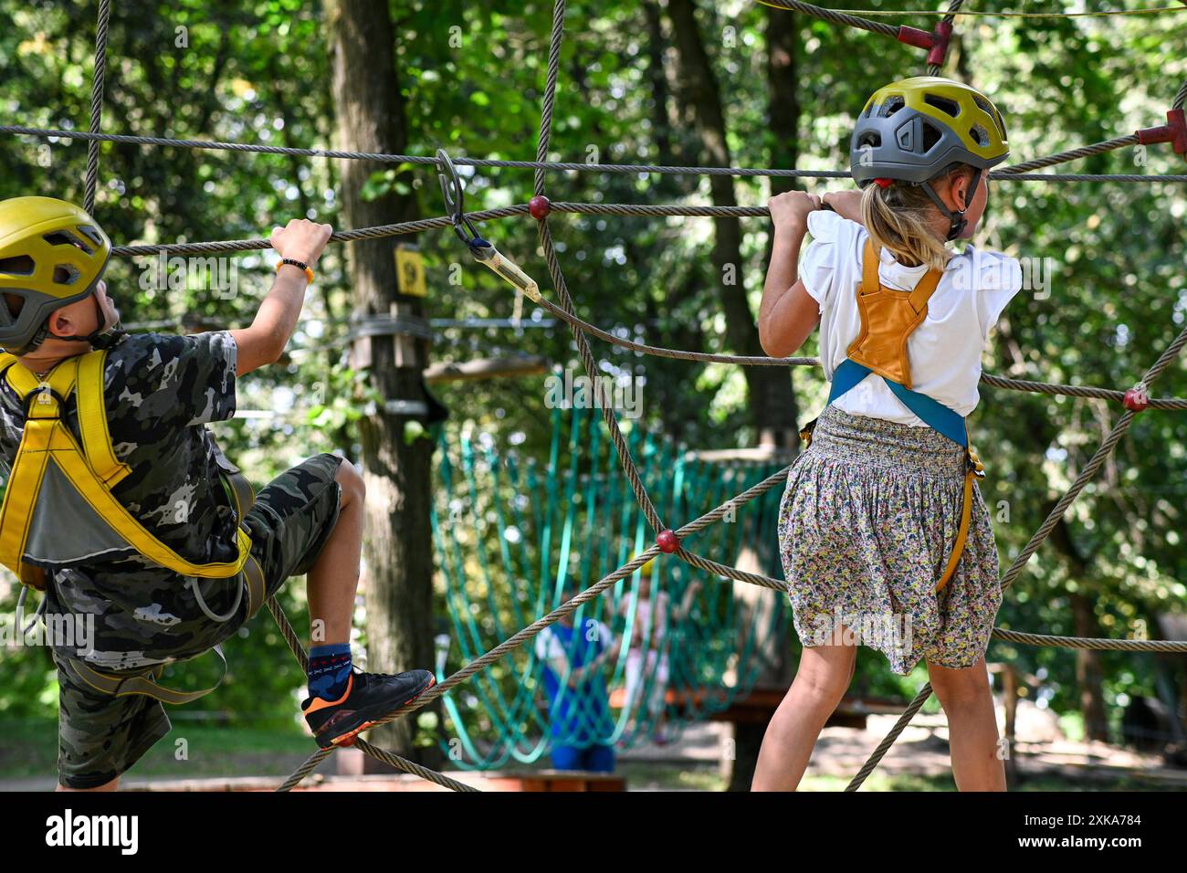 Two children wearing safety harnesses and helmets navigating a rope ...