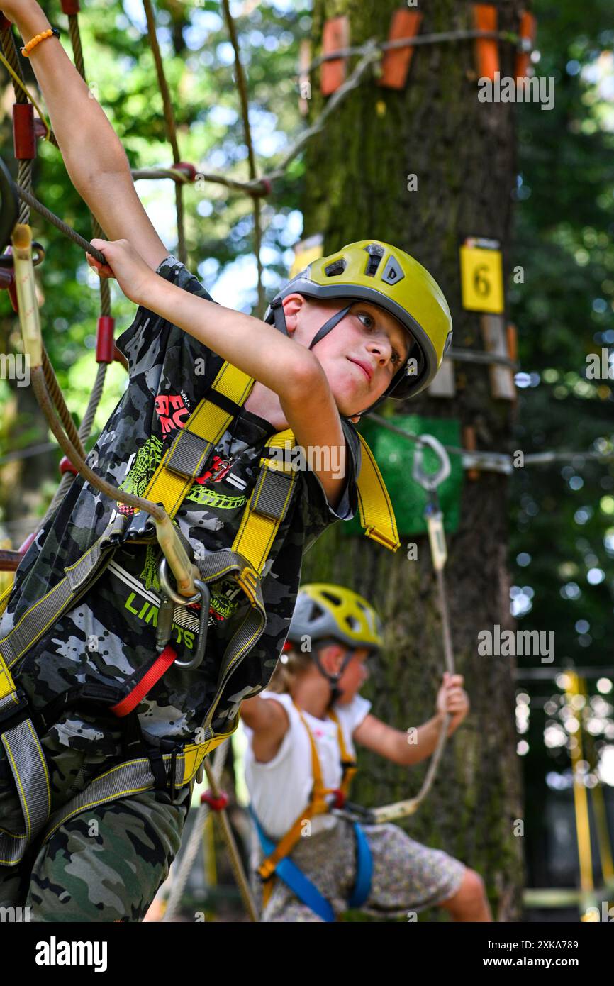 Two children wearing safety harnesses and helmets navigating a rope ...