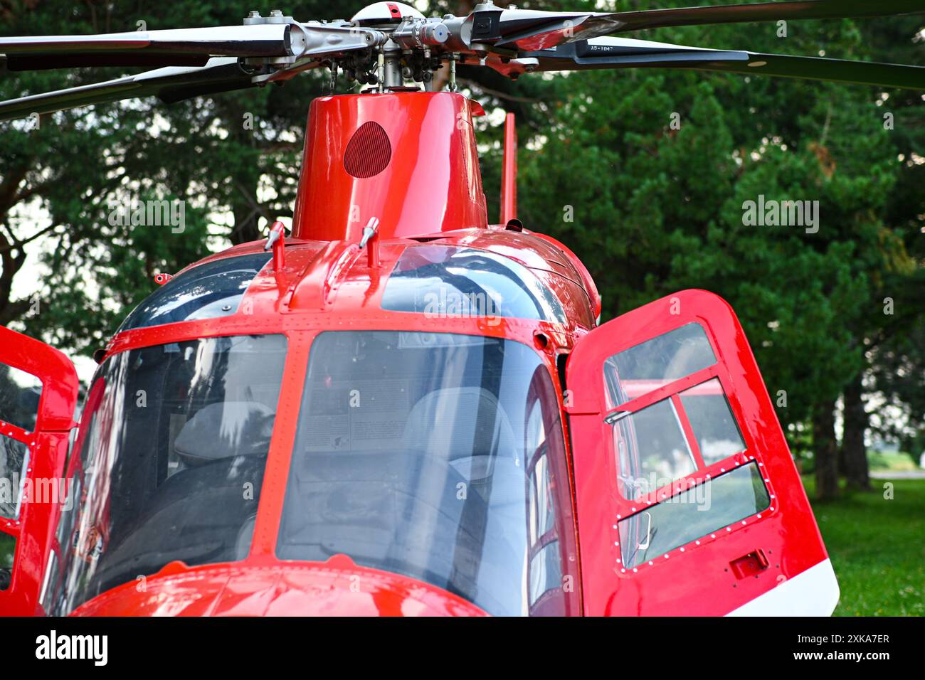 rescue red helicopter standing on the grass near the trees on a sunny ...