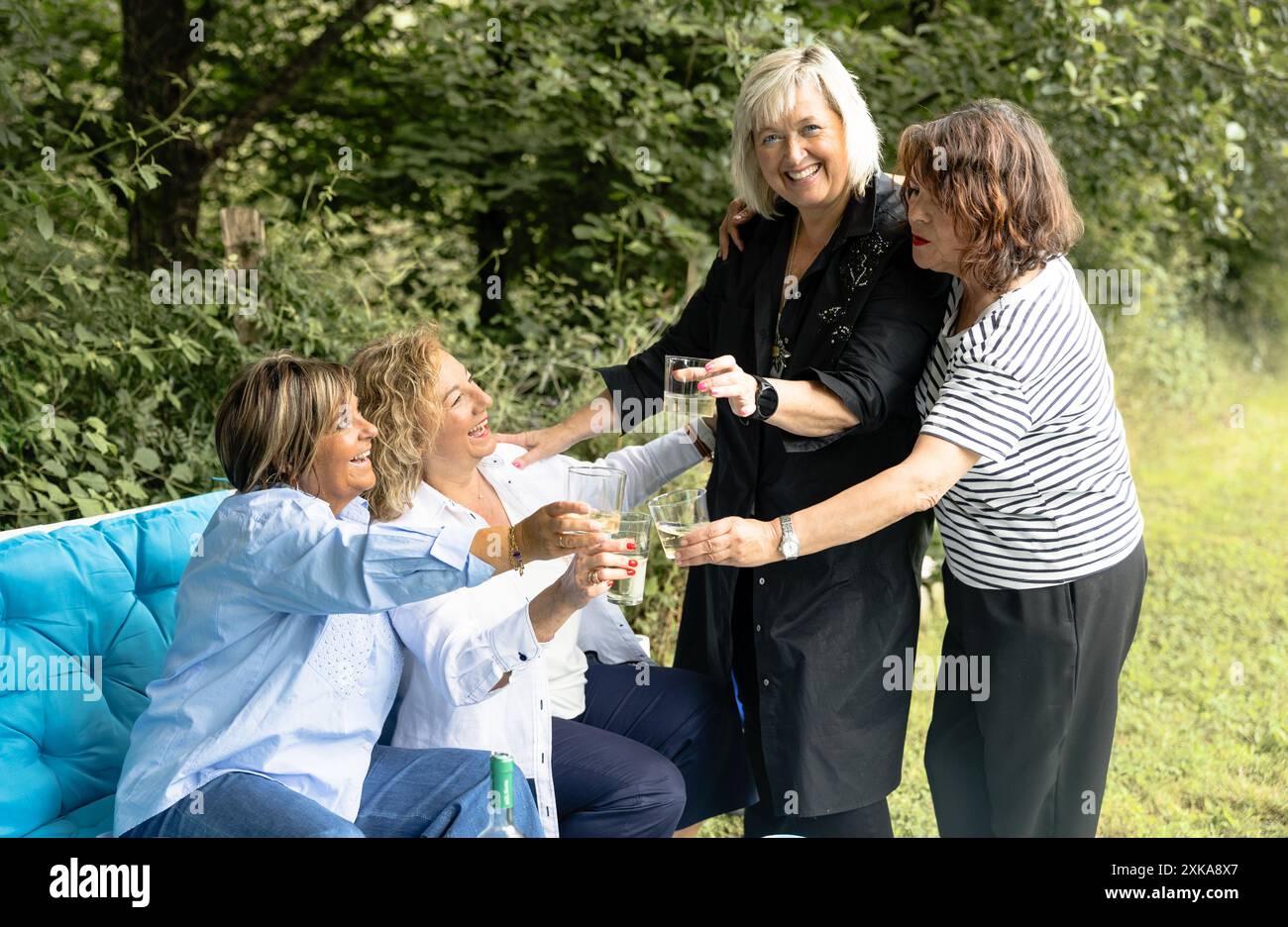 Four mature women friends raising their glasses in a toast, happily ...