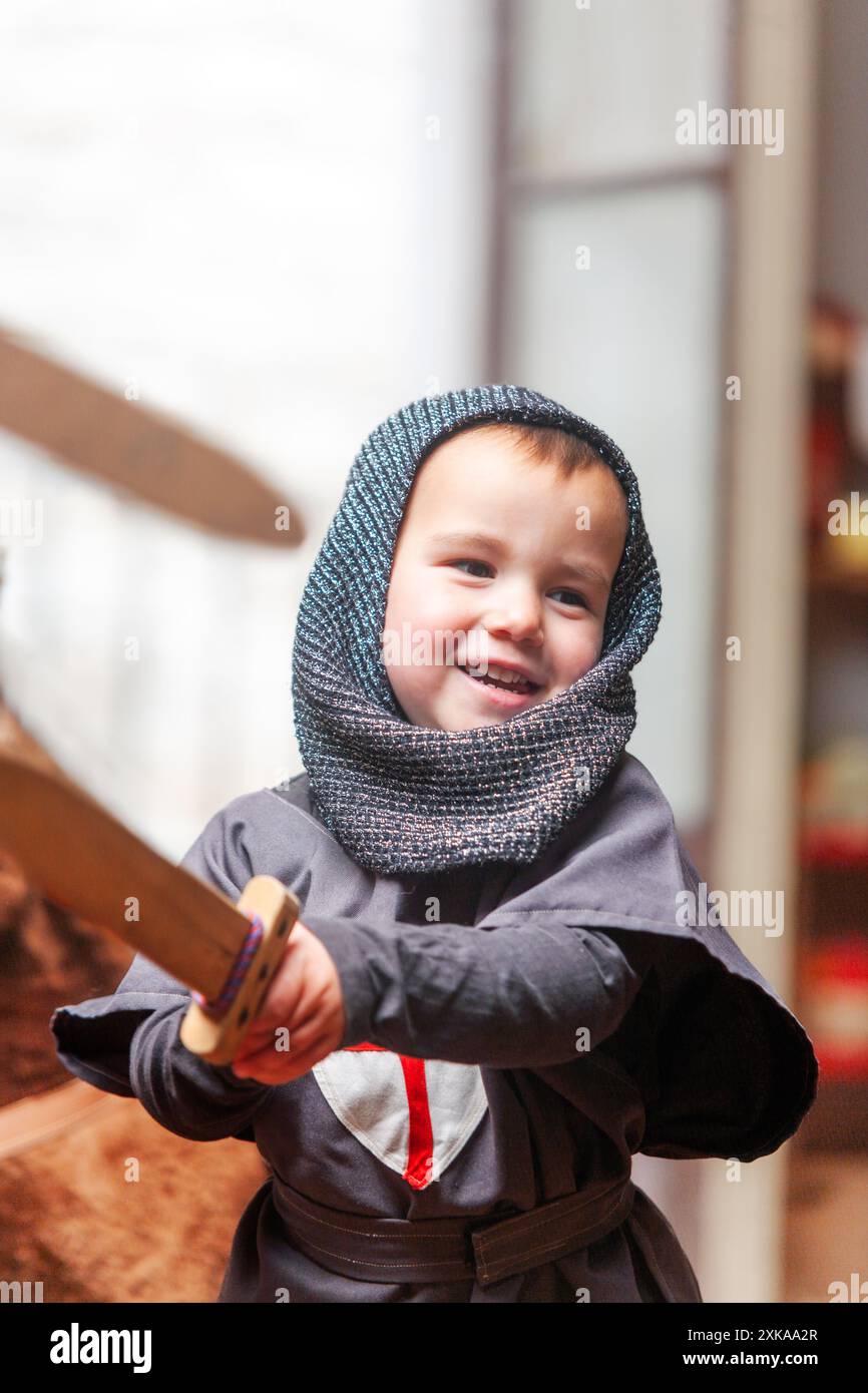 A kid is dressed in a knight costume and holds a wooden sword while ...