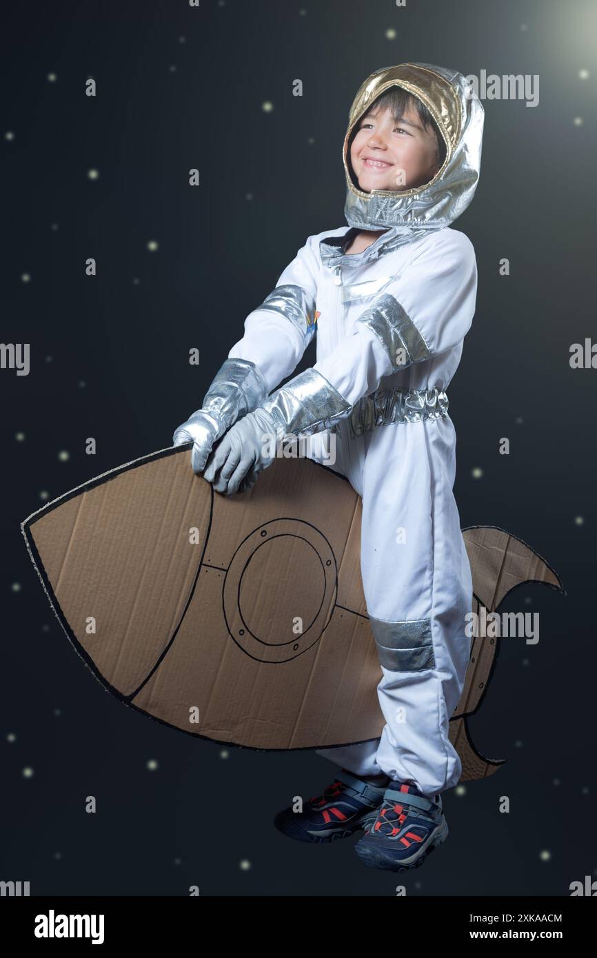 A smiling kid in a space suit riding a cardboard rocket traveling ...