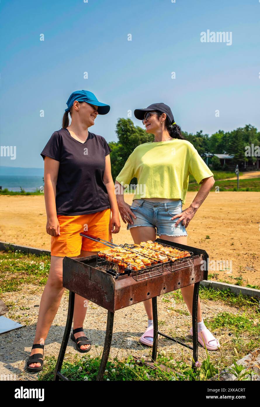 Two russian woman talking and cooking pork bbq on the beach of Japanese ...