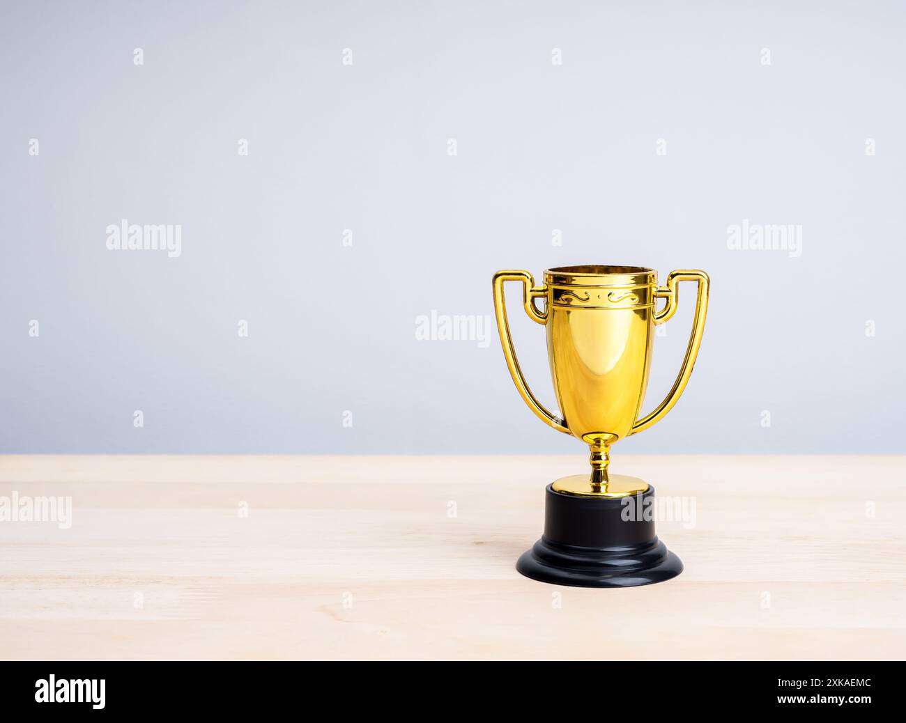 A small gold trophy, brass steel, dual handle isolated on wooden table ...