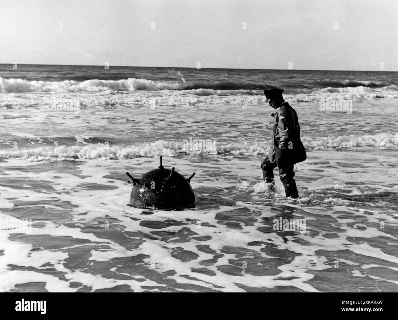 A German soldier approaches a sea mine washed up on the beach. Undated ...