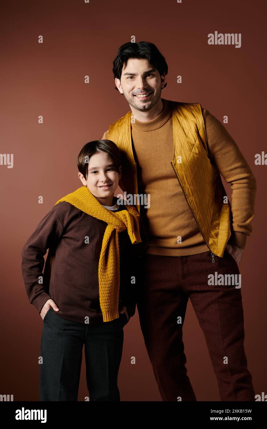 A father and son pose together in a studio setting, both wearing brown ...