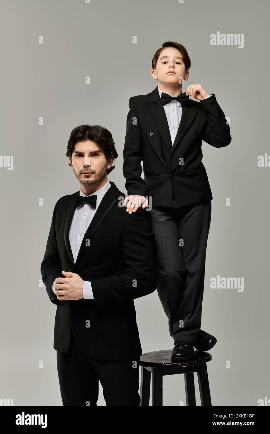 A father and son in formal wear stand together against a grey backdrop ...
