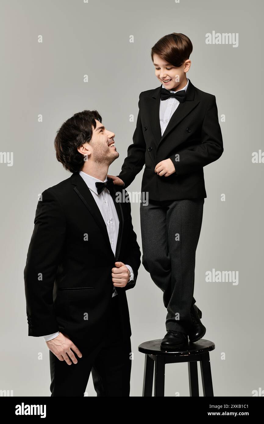 A father and son, both dressed in suits and bow ties, share a playful ...