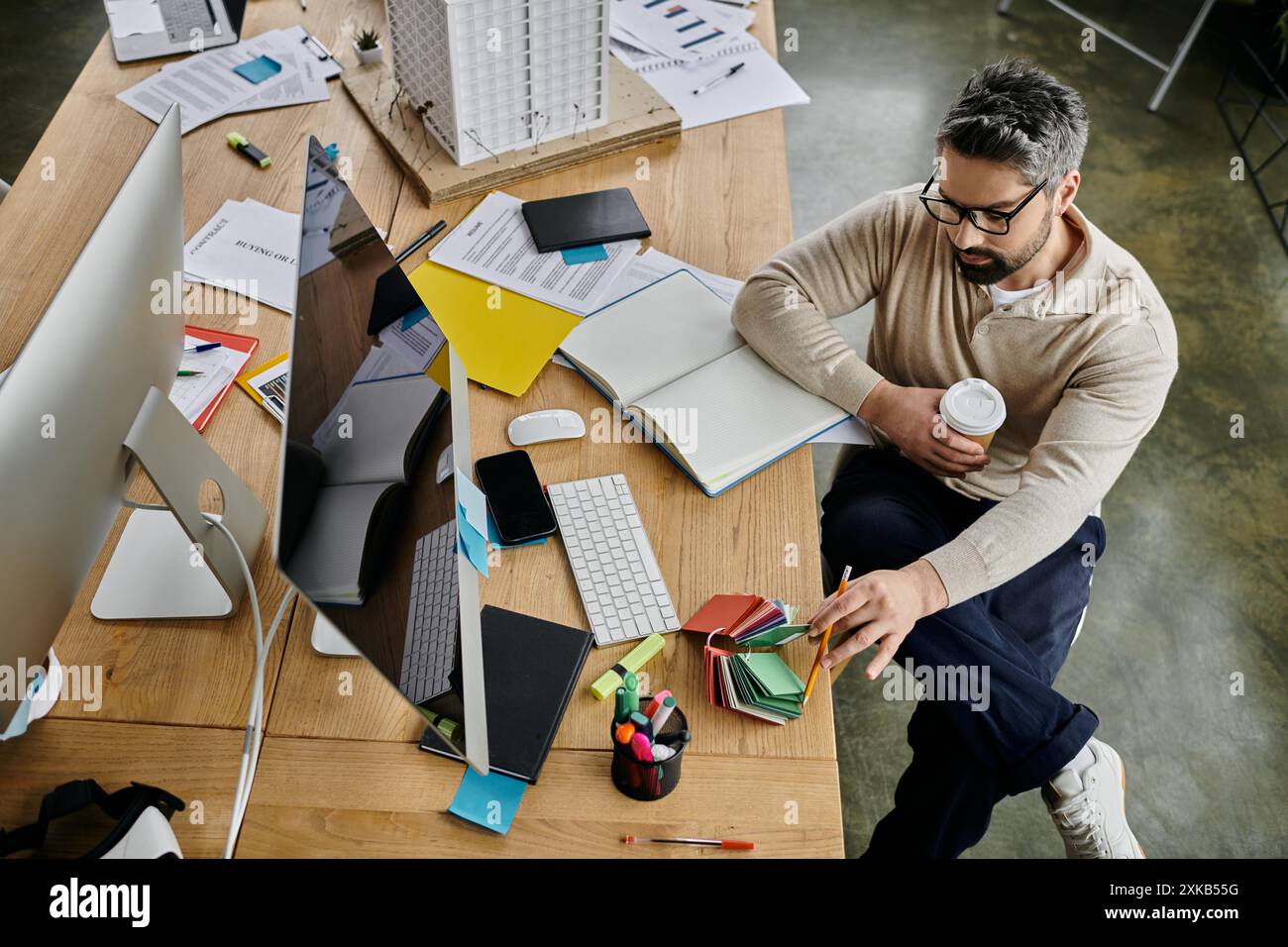 A handsome businessman with a beard sits at a cluttered desk in a ...