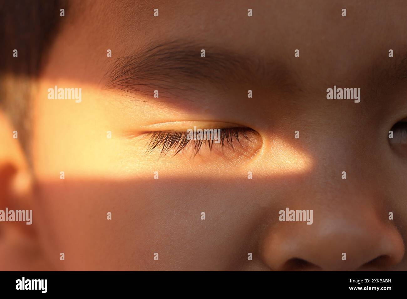 Lovely boy with closed eyes and evening sunlight hit the face, making ...