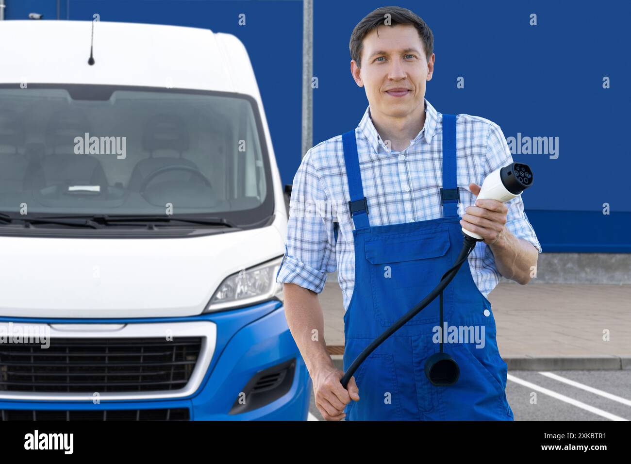 Man in uniform holds electric vehicle charging plug. Electric vans in ...