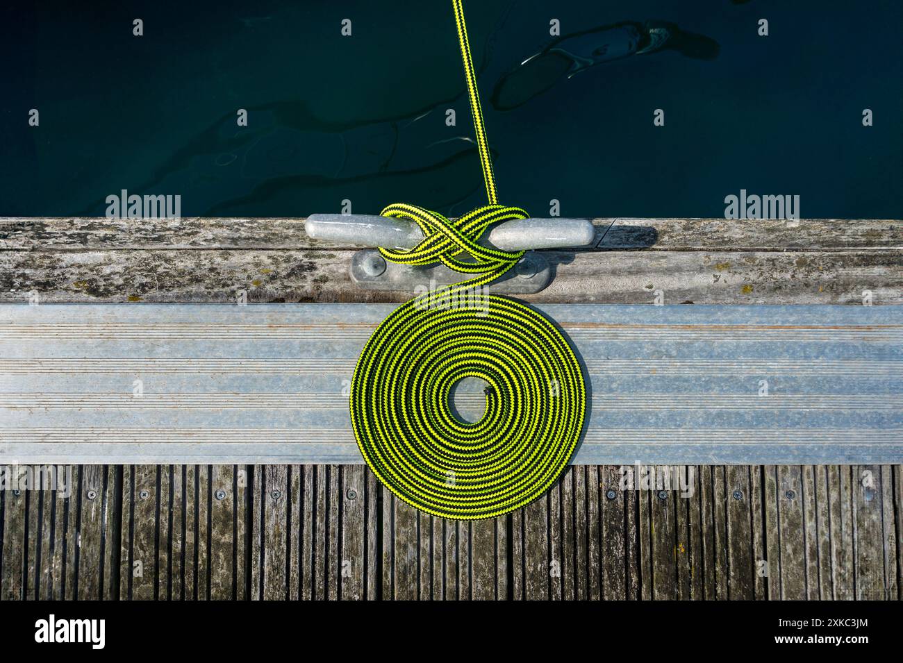 Coil of yellow mooring rope on a wooden quayside with a cleat Stock ...