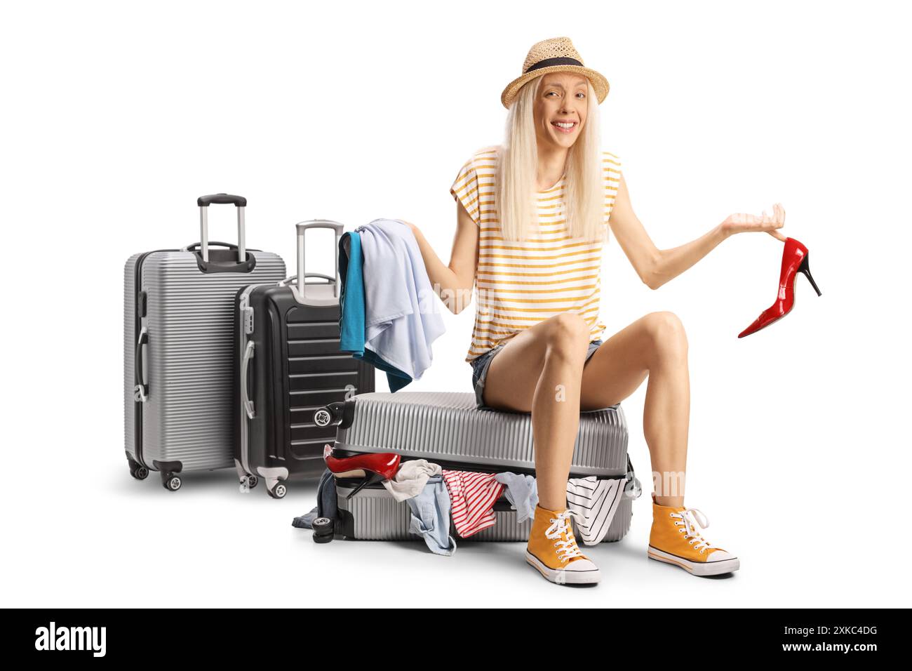 Young woman sitting on an overpacked suitcase and holding high heels ...