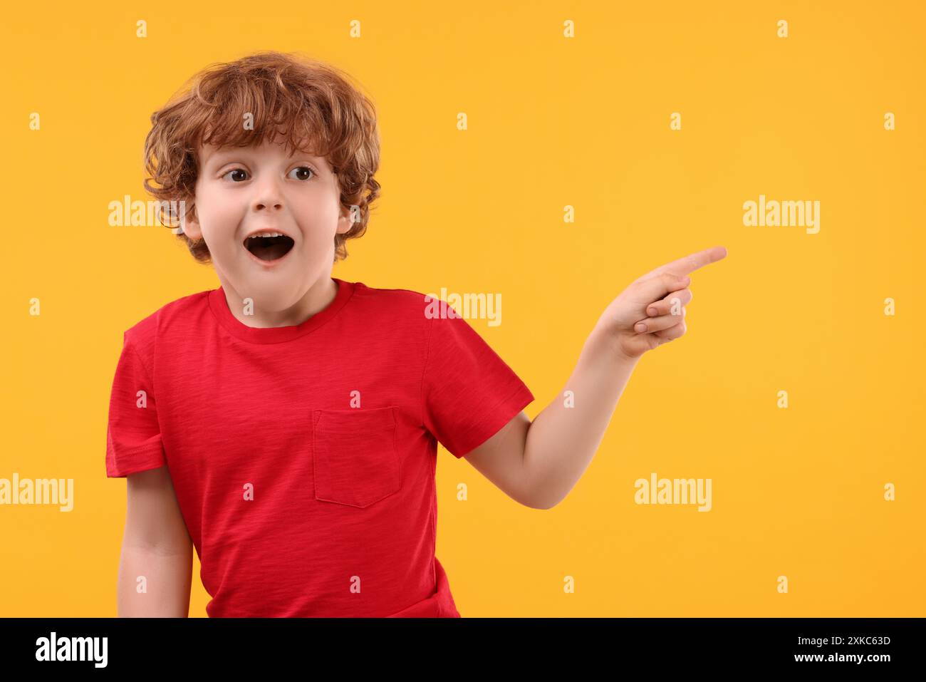 Portrait of emotional little boy pointing at something on orange ...