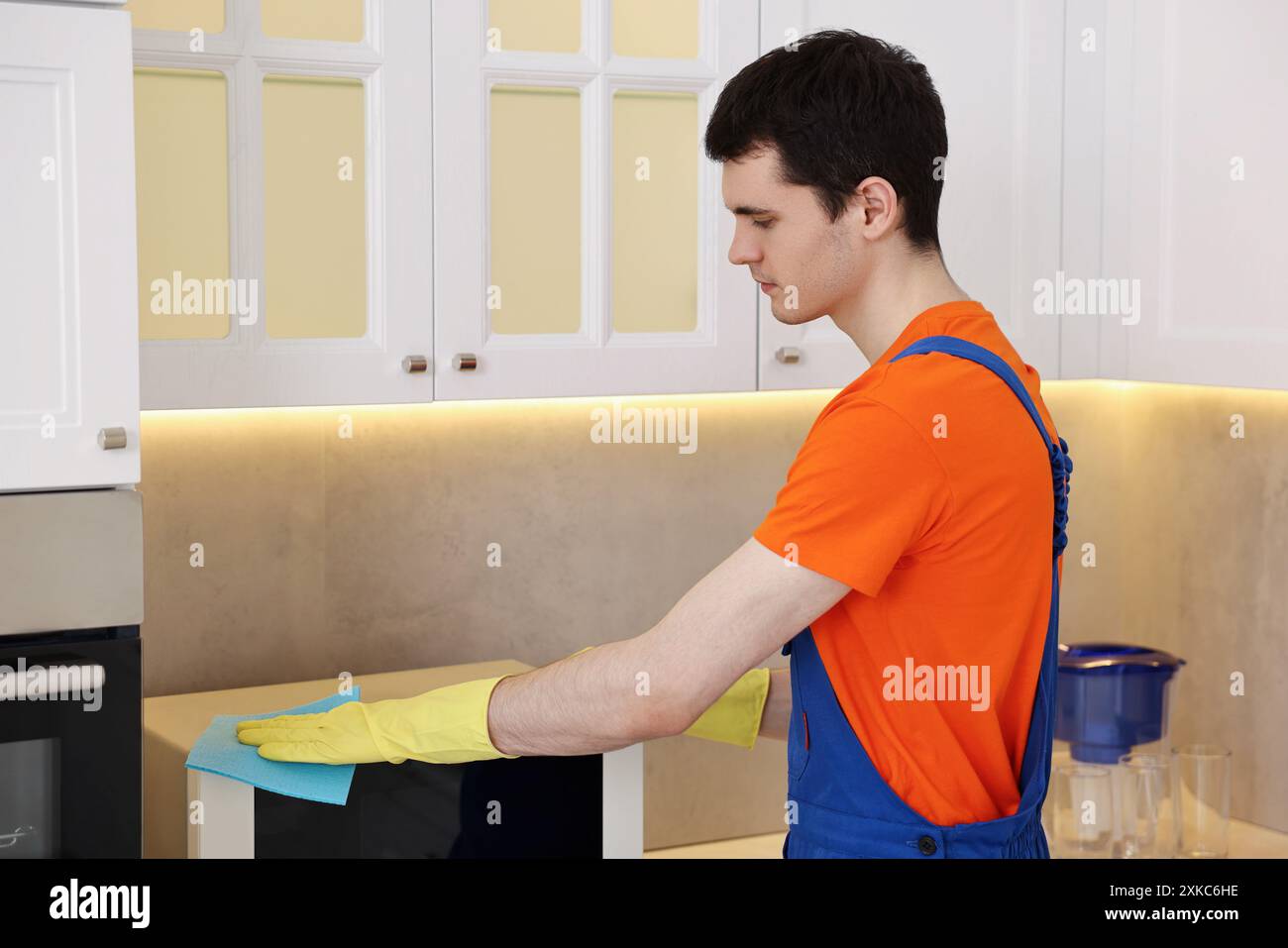 Professional janitor wearing uniform cleaning microwave oven in kitchen ...