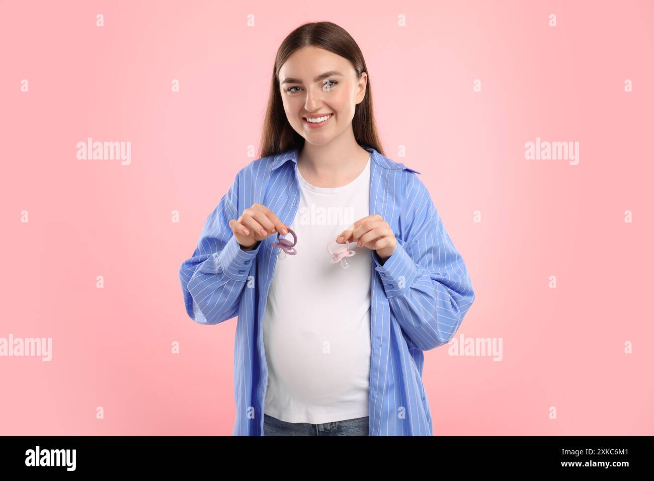 Expecting twins. Pregnant woman holding two pacifiers on pink ...