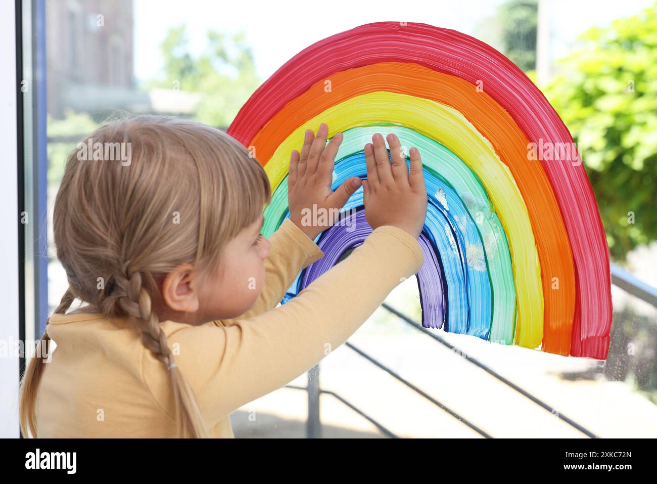 Little girl touching picture of rainbow on window indoors Stock Photo ...