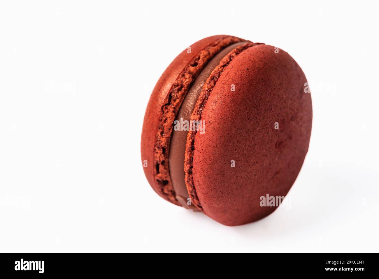 A single, red macaron with a strawberry filling is shown in a close-up ...