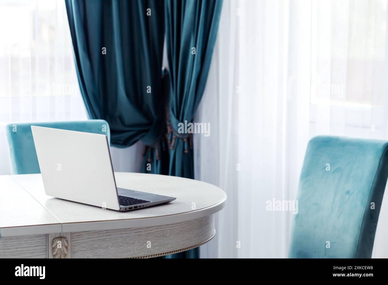 A modern workspace featuring a sleek laptop, elegant blue curtains, and ...