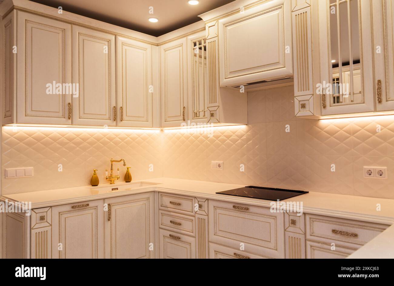 Elegant white kitchen with gold-accented cabinets and modern lighting ...