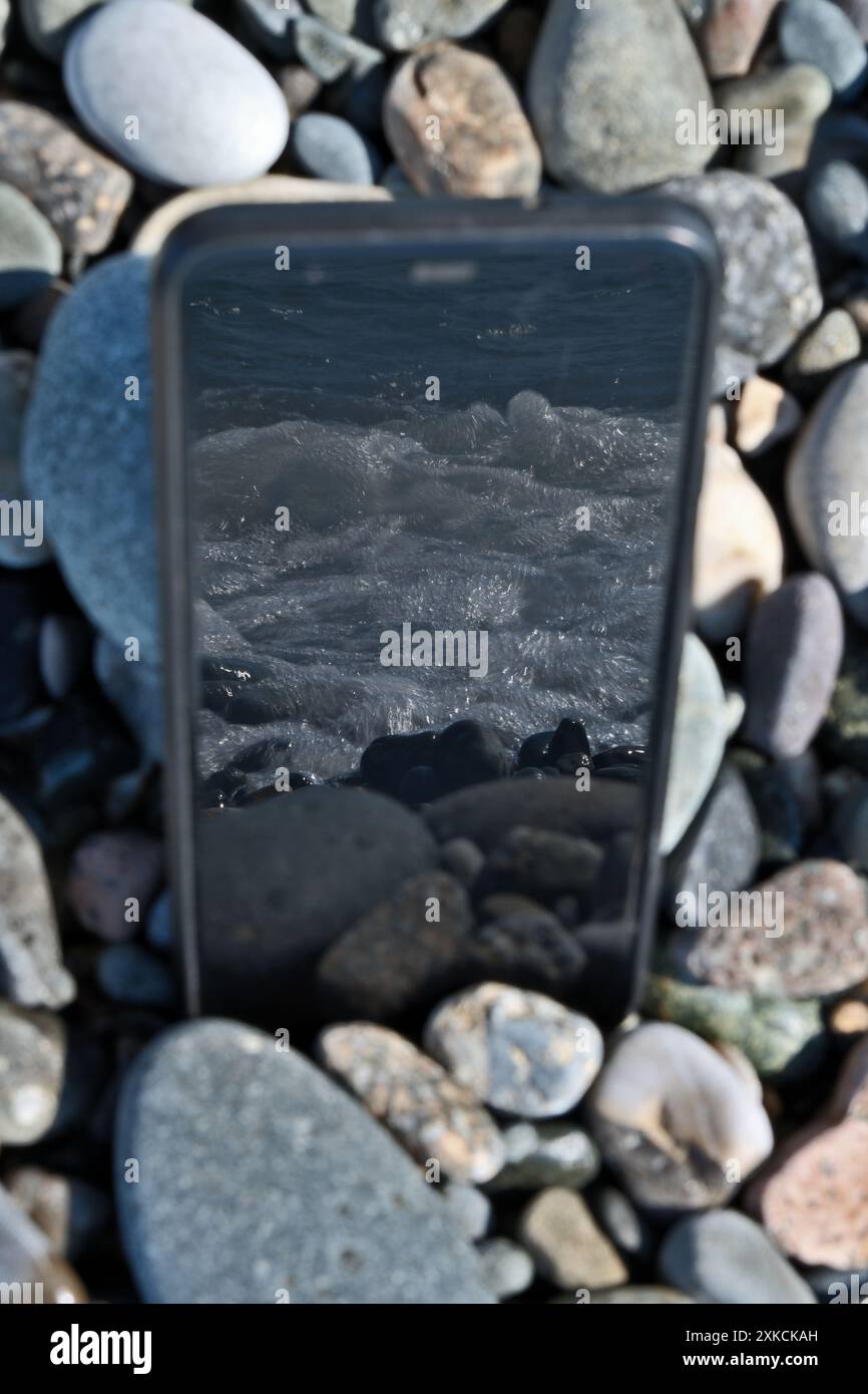 Mobile phone with a reflection of the sea on a pebble beach Stock Photo ...