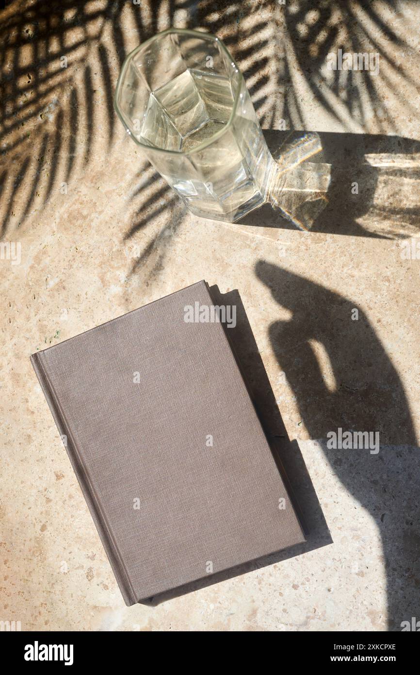 Book and Glass on Sunny Table. A brown book and a glass of water on a ...
