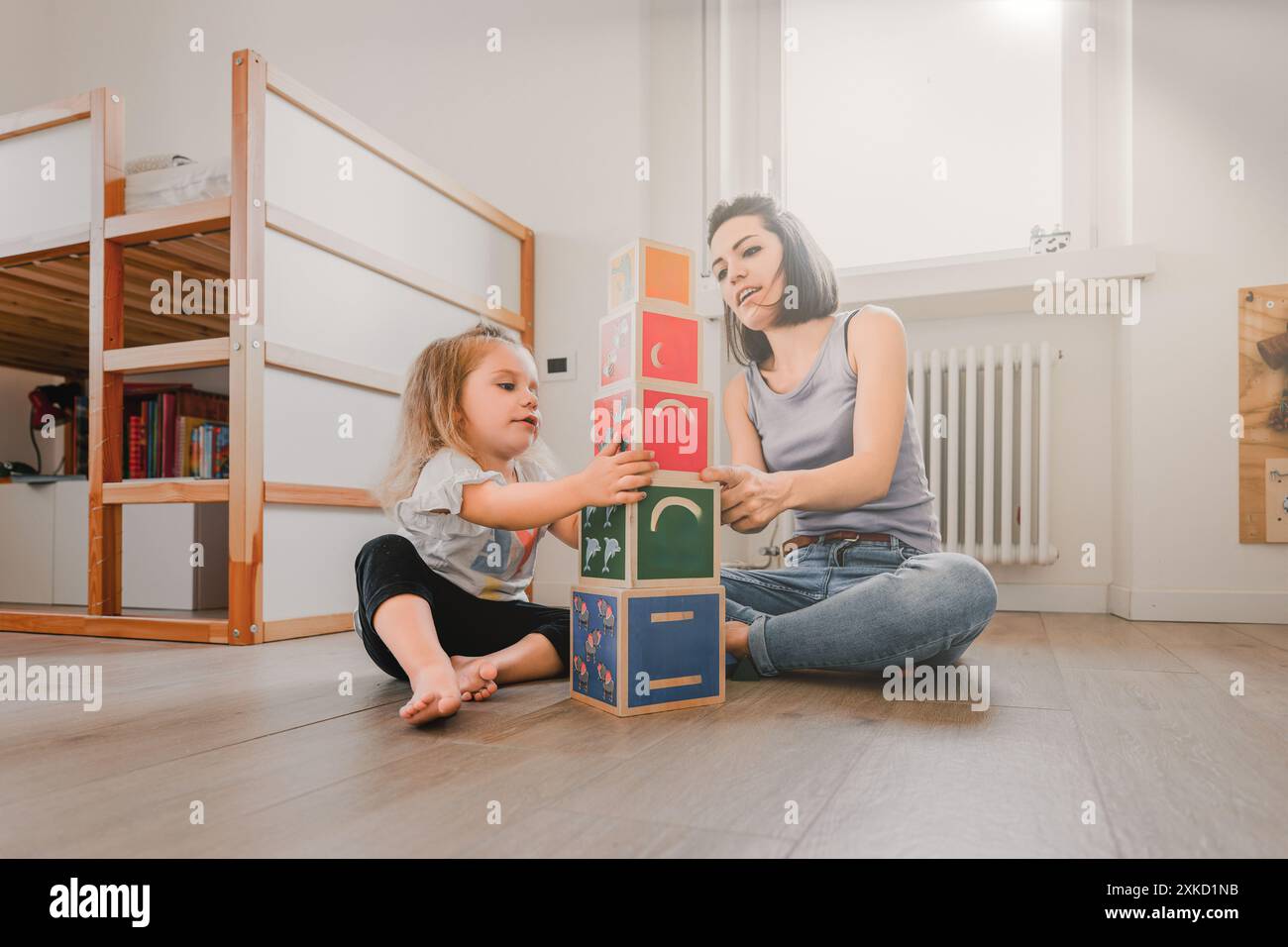 Mother and daughter happily play with colorful blocks in their cozy playroom, bonding and ...