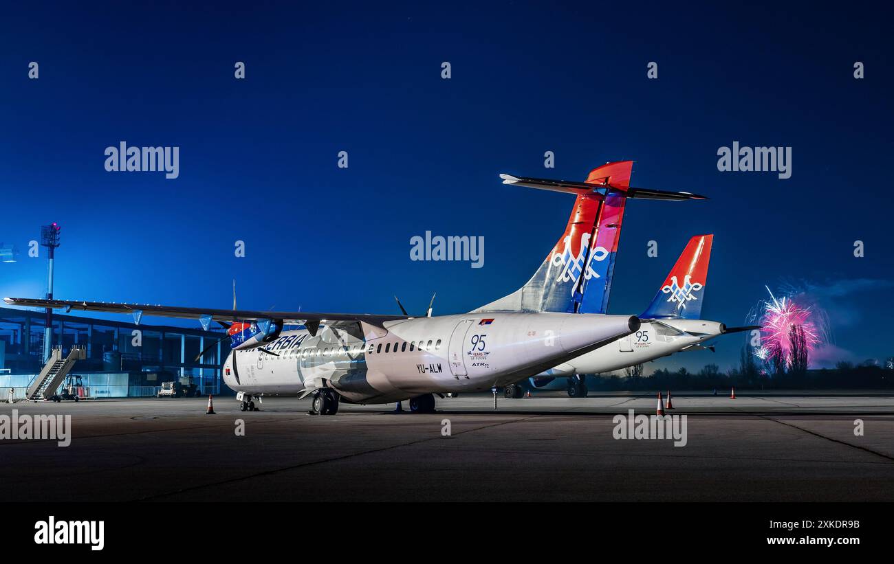An airplane with a white body and red tail is parked on a tarmac at ...