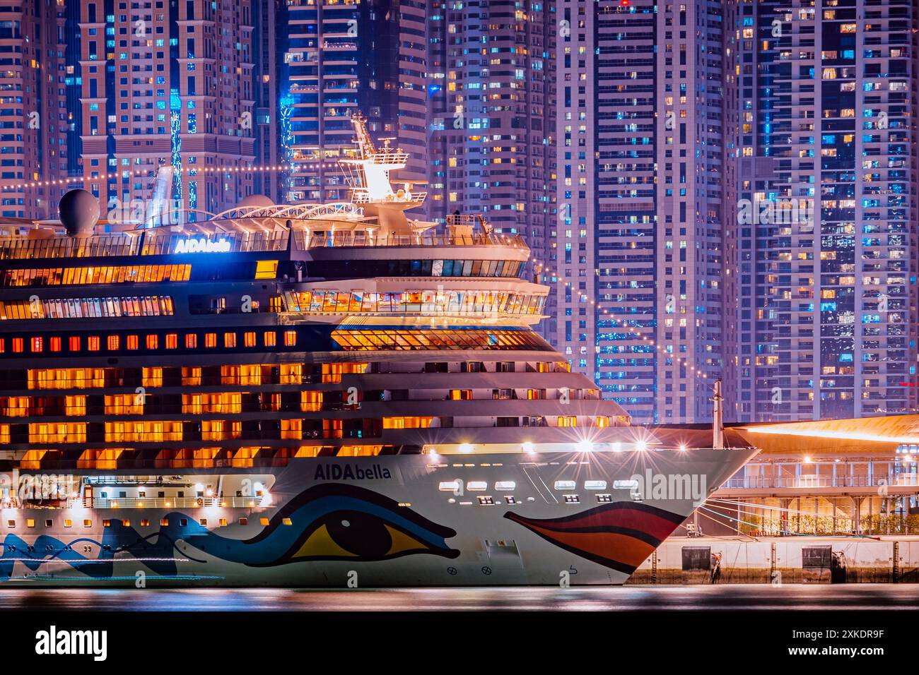 A large cruise ship is docked in Dubai at night, with the city's ...