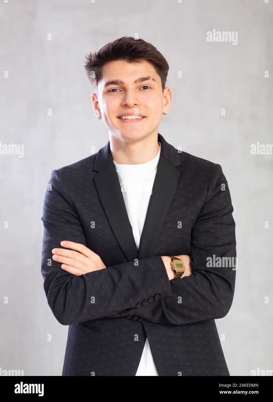 Positive male student in black jacket poses with folded arms on chest ...