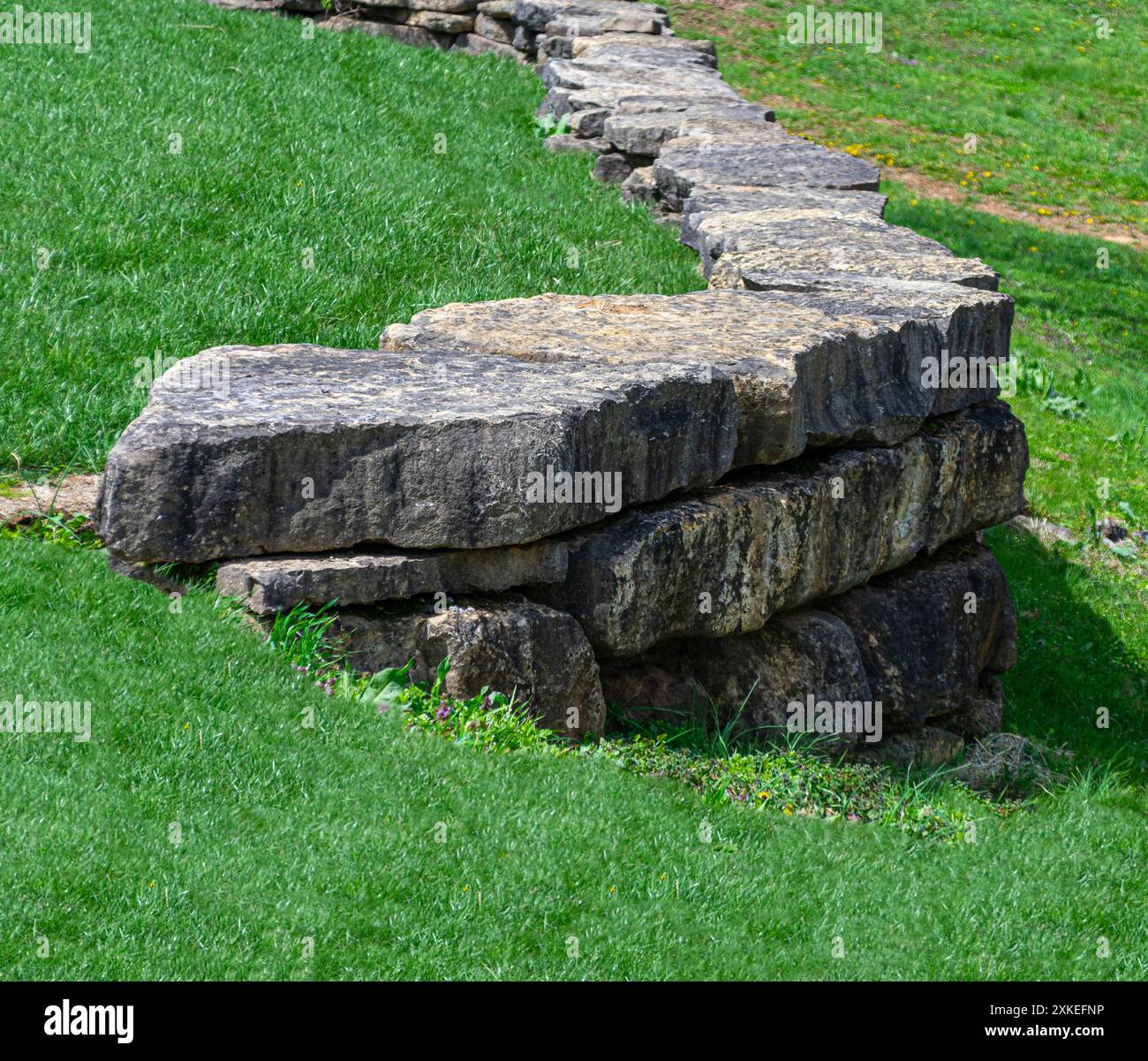 Retaining wall made of stacked flat rocks through green grass Stock ...