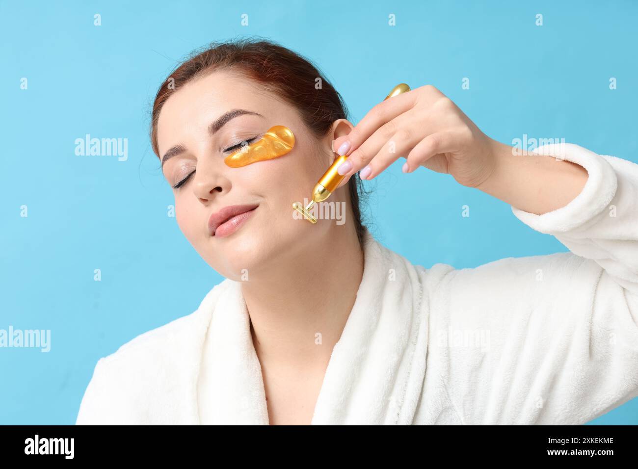 Beautiful young woman with under-eye patches using facial massage tool ...