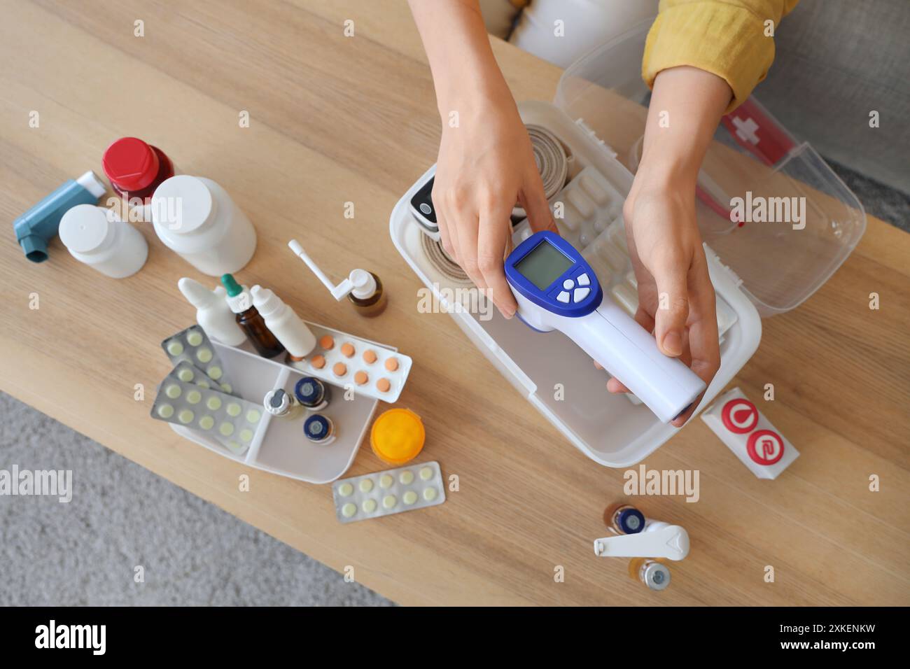 Woman putting infrared thermometer in first aid kit at home, top view ...