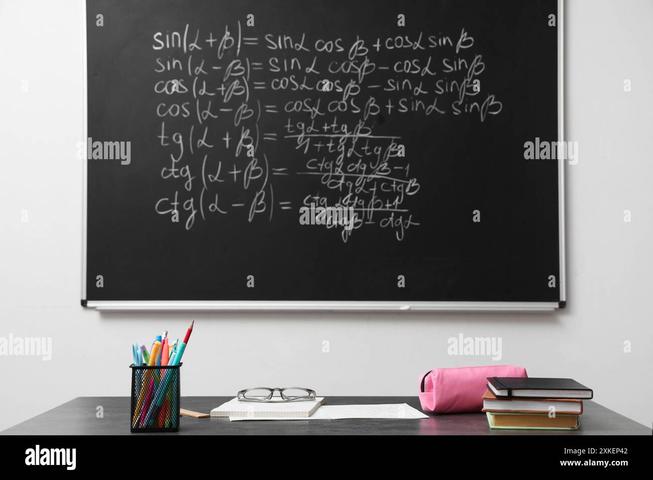 Stationery on desk and blackboard with math formulas hanging on light ...