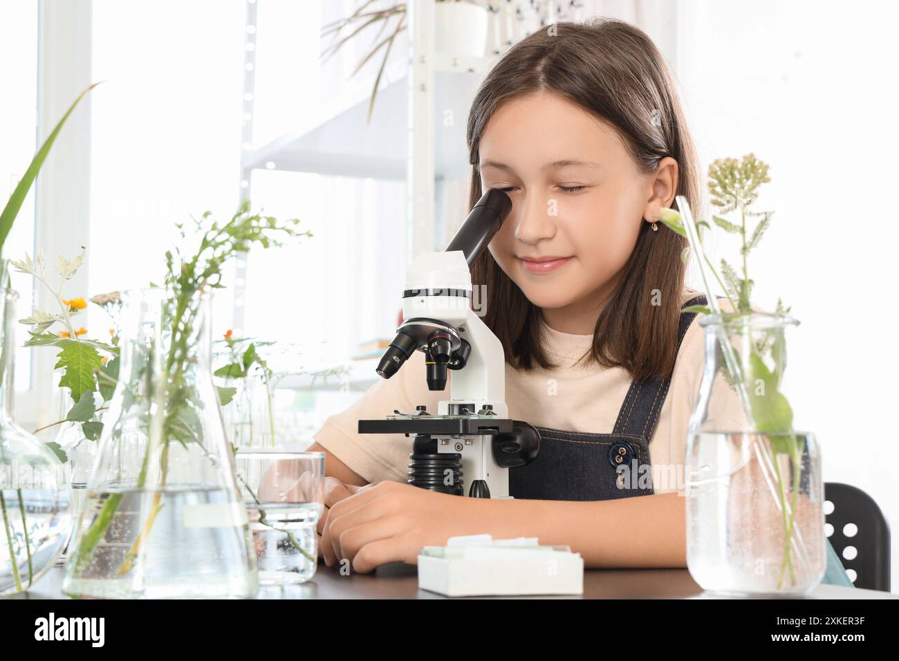Teenage girl looking through microscope in Biology class at school ...