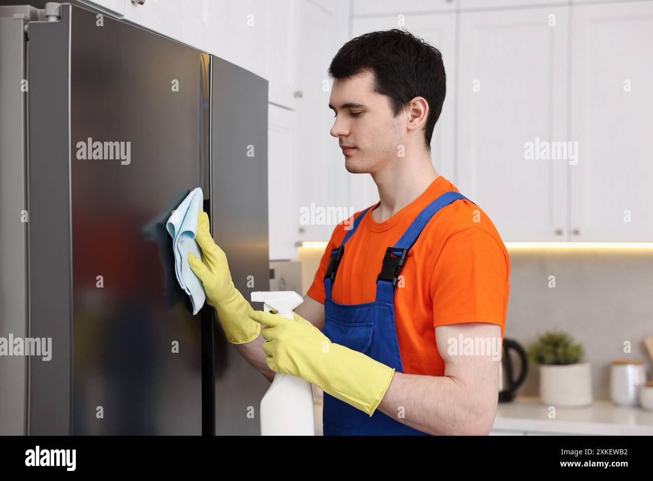 Professional janitor wearing uniform cleaning fridge in kitchen Stock ...