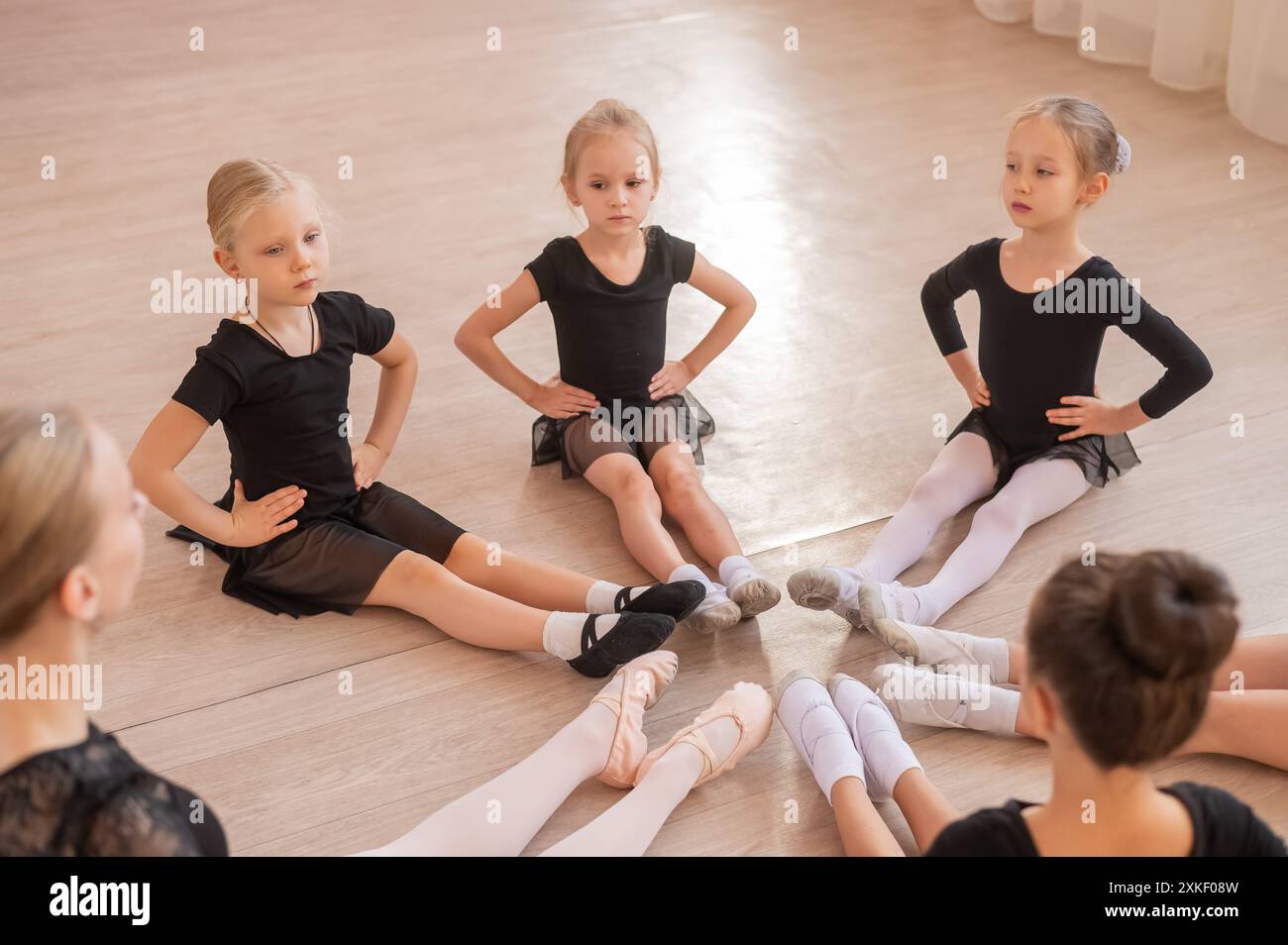 Caucasian woman and five little girls sit in a circle and do stretching ...