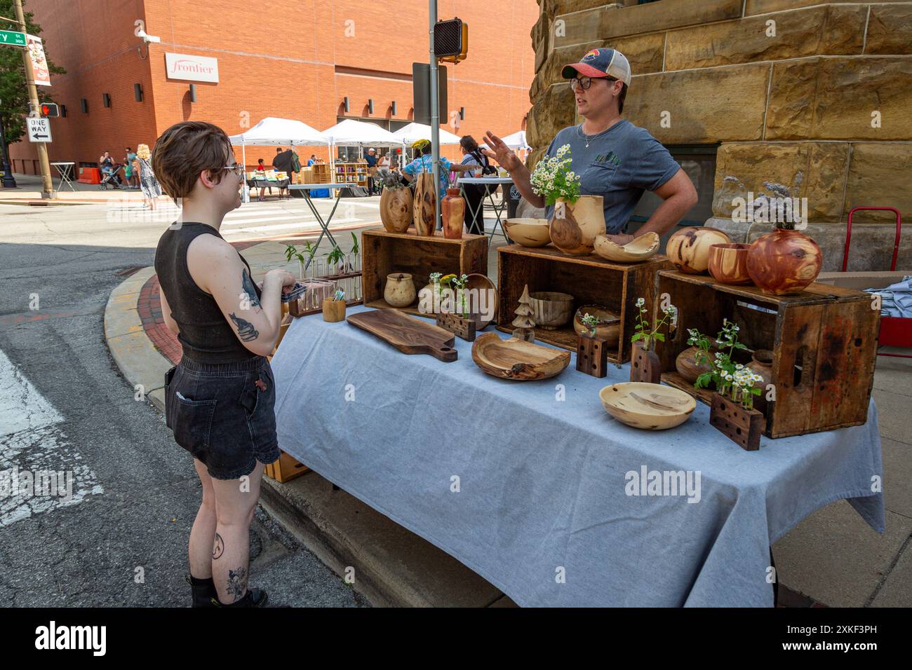 A woman stands behind a vendor stall displaying wooden bowls and vases ...