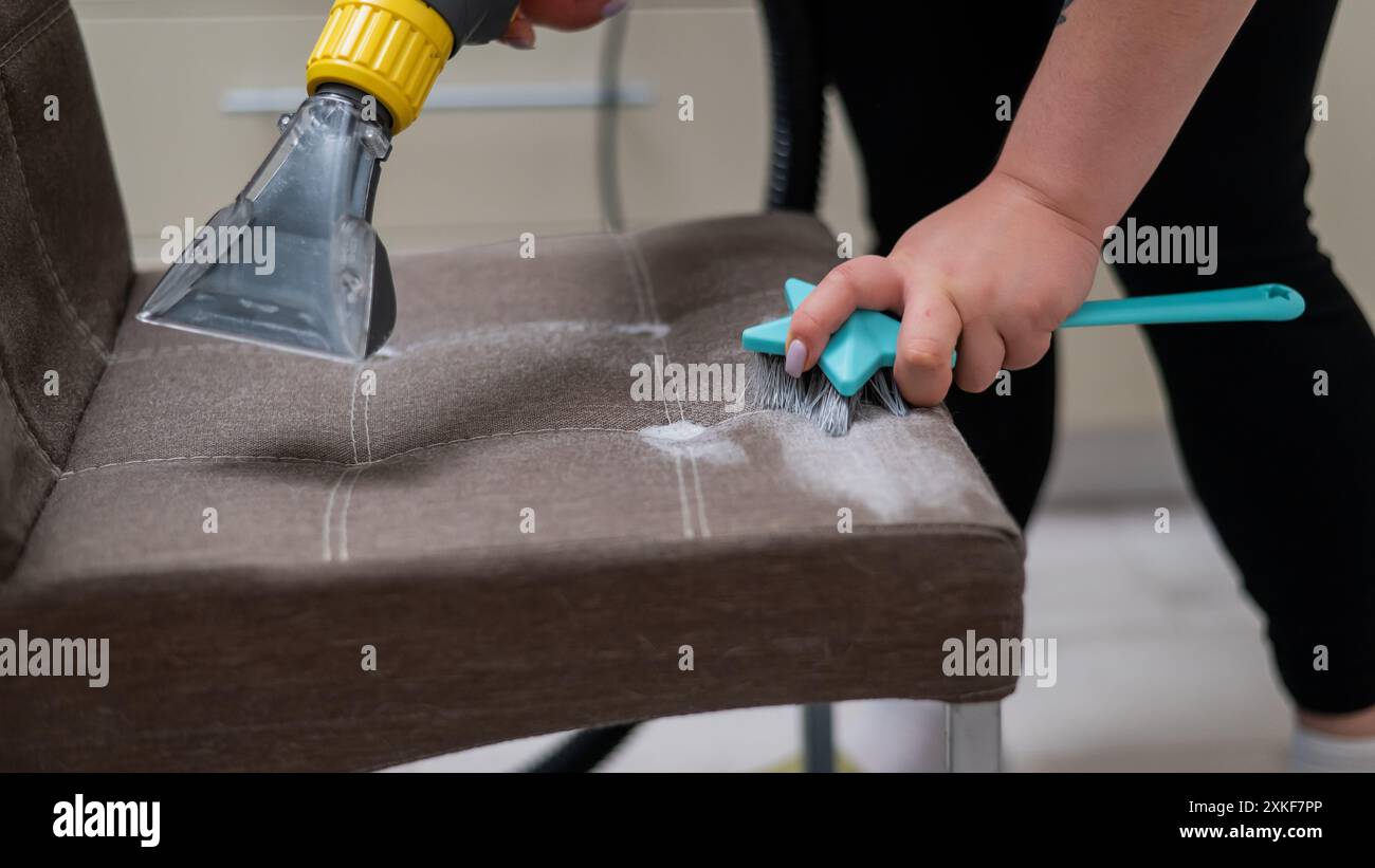 Woman cleaning a fabric chair using a professional washing vacuum ...