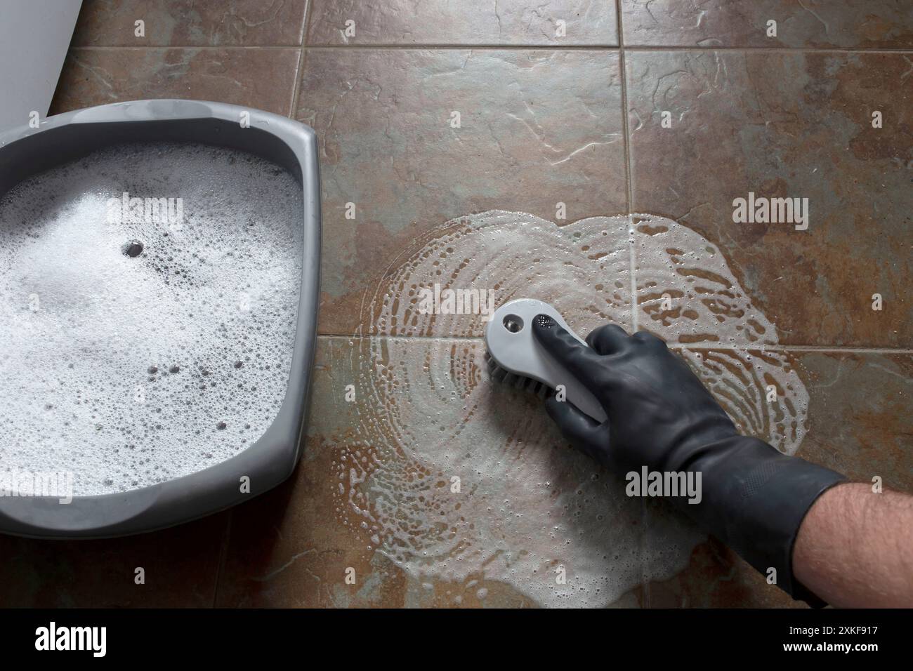 Person scrubbing kitchen floor tiles with a scrubbing brush and soapy ...