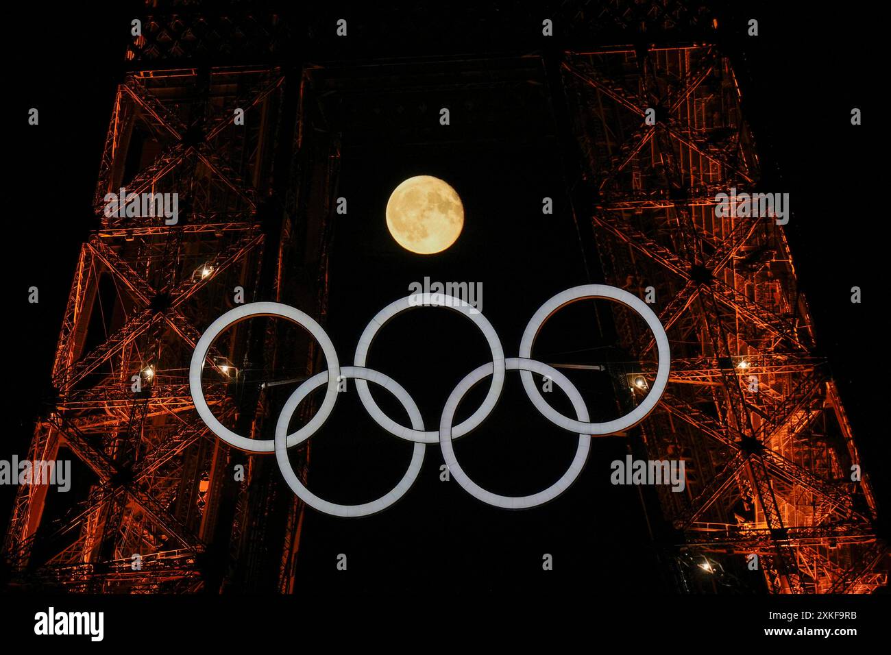 A full moon rises behind the Olympic rings hanging from the Eiffel ...