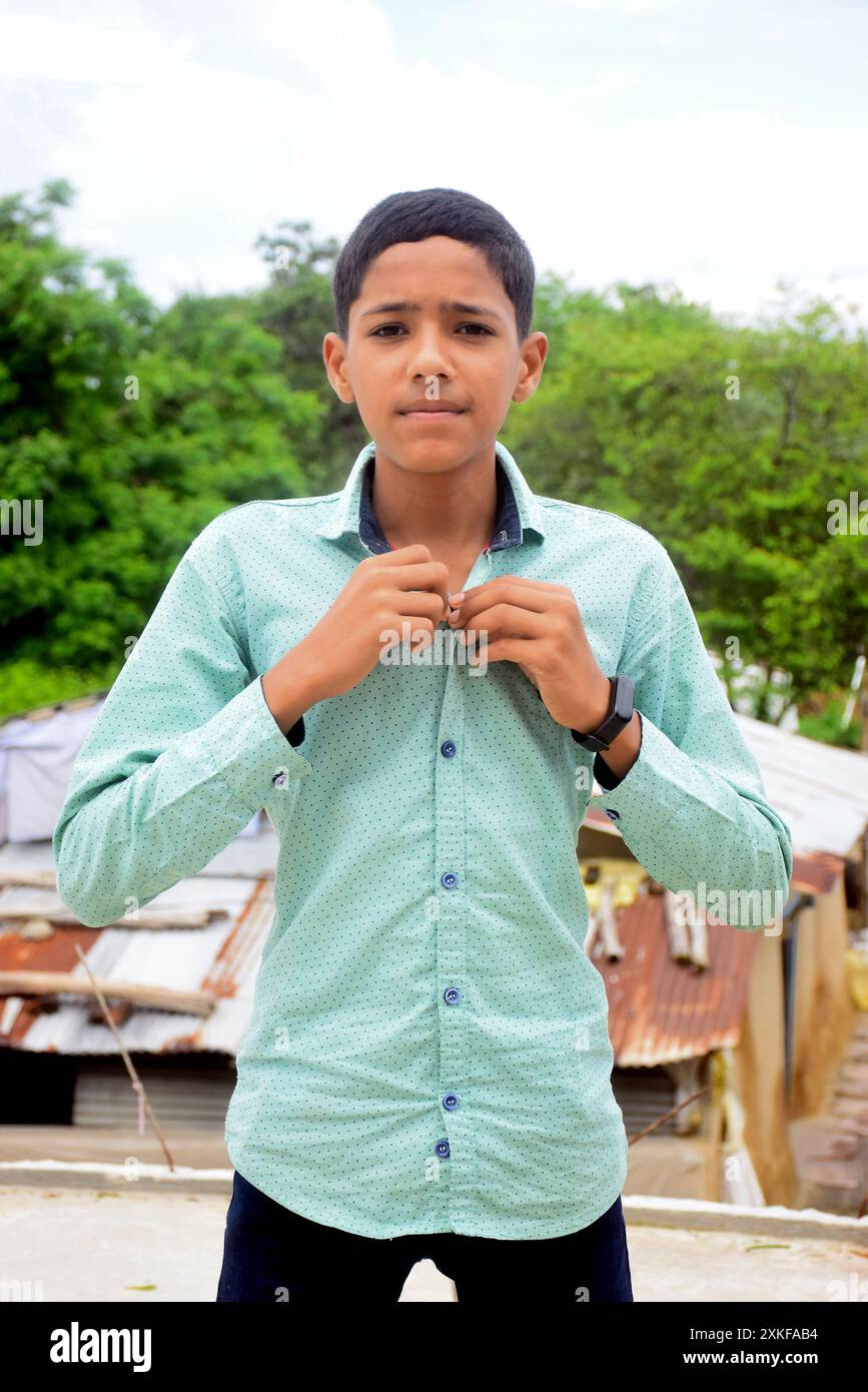 a boy buttoning their shirt with village background Stock Photo - Alamy